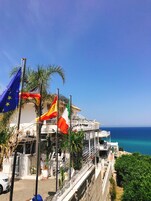 Um edifício costeiro com várias bandeiras, incluindo a bandeira da União Europeia, e vista para o mar.