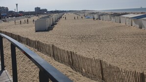 Uma praia com uma fileira de cabanas e uma cerca em primeiro plano.