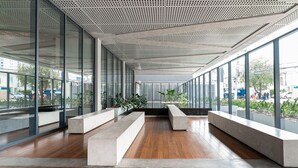 Um interior moderno com piso de madeira, bancos de concreto e janelas amplas com vista para o exterior.