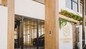 Uma entrada de edifício moderna com porta de vidro, um pilar de madeira e uma placa com a inscrição "EL ENCANTO PLAYA SUR".