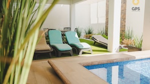 Área da piscina com espreguiçadeiras e um pequeno jardim.
