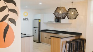Uma cozinha moderna com uma ilha central, banquetas, geladeira e micro-ondas.