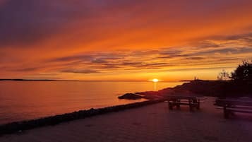 Um pôr do sol sobre águas calmas, com um calçadão pavimentado e bancos.