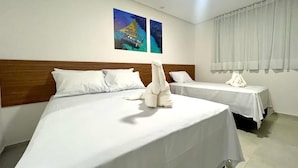 Quarto de hotel com duas camas, roupa de cama branca, cabeceira de madeira e um quadro na parede.