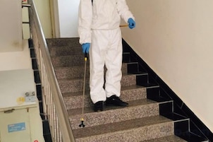 Uma pessoa vestida com um terno branco e luvas azuis, em um lance de escadas.