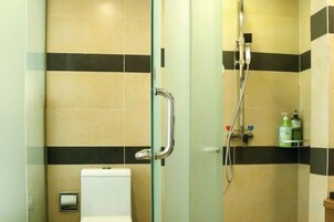 Divisória de chuveiro com vidro, vaso sanitário e barra de apoio, além de prateleira com artigos de higiene pessoal.