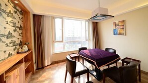 Quarto de hotel com cama, escrivaninha, cadeira, mesinha e janela com cortinas.