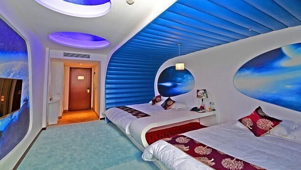Quarto moderno com paredes curvas, um claraboia circular e cama com colcha estampada em vermelho e branco.