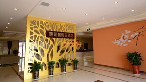 Uma área de recepção de hotel com divisória amarela decorativa, plantas em vasos e uma parede com design floral.