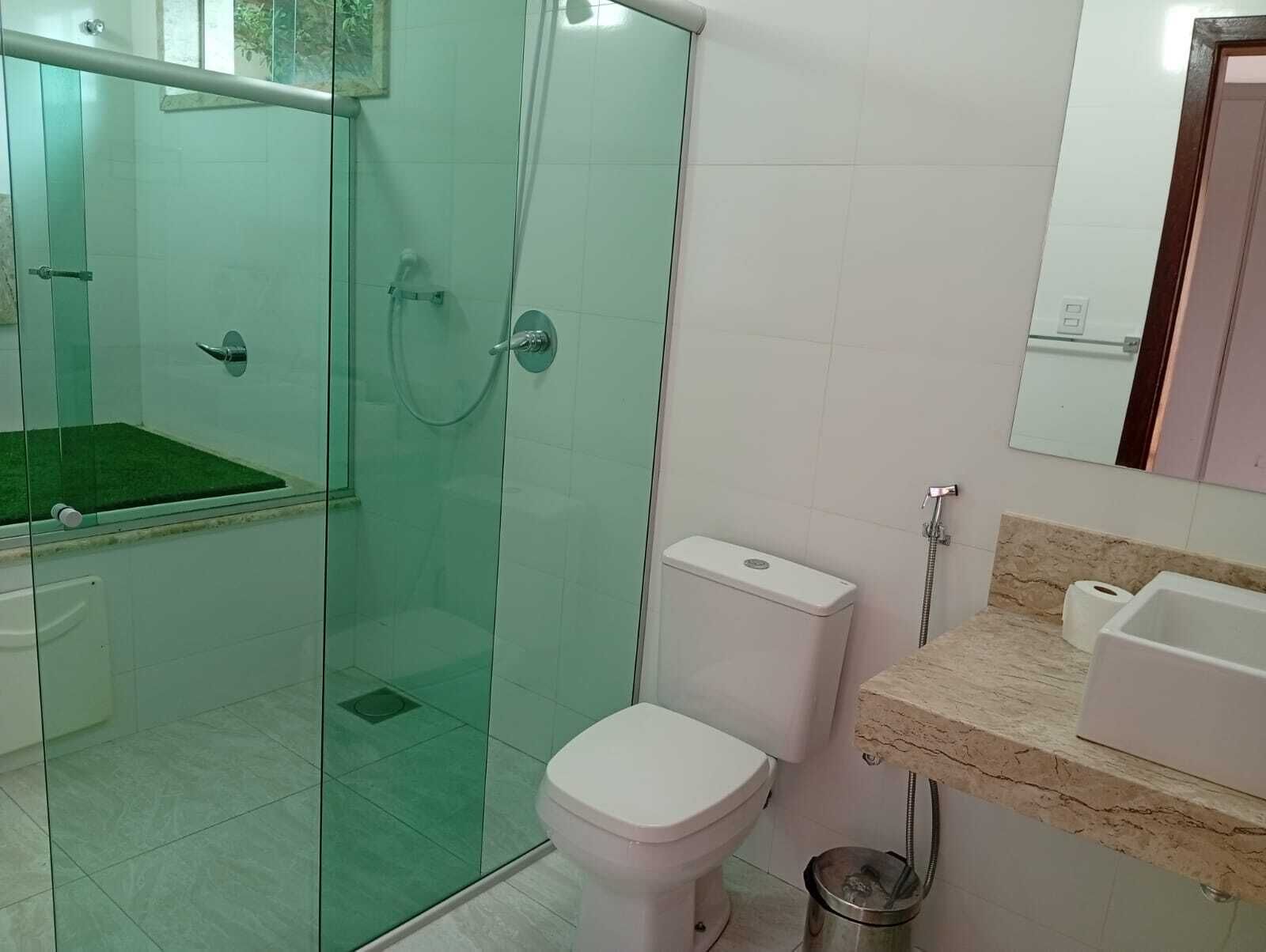 Casa de banho com cabine de chuveiro em vidro, sanita e lavatório com bancada de mármore.