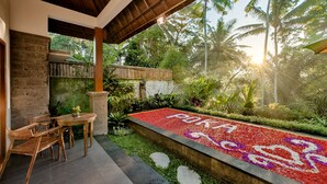 Área externa com mesas e cadeiras, parede decorativa e jardim com um canteiro de flores formando a palavra 'PUKA'.