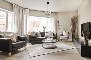 Uma sala de estar moderna com sofá, poltrona, mesa de centro e uma grande janela com cortinas.