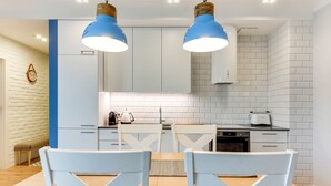 Uma cozinha moderna com armários brancos, uma mesa de jantar de madeira e luminárias pendentes azuis.