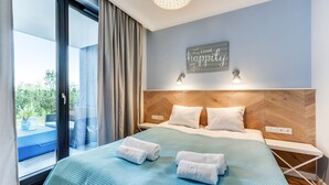 Quarto de hotel moderno com uma cama grande, duas mesas de cabeceira, uma luminária na parede e vista para o exterior.