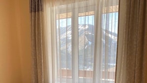 Quarto com cama, mesa de cabeceira, luminária e janela com cortinas.