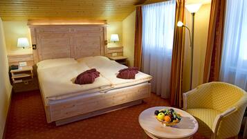 Quarto de hotel com uma cama grande, duas luminárias de cabeceira, uma mesinha com uma cesta de frutas e uma cadeira.