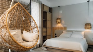 Quarto moderno com cadeira suspensa, cama e duas luzes pendentes.