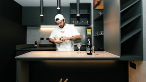 Uma área de bar com um balcão identificado como "Marshall", uma pessoa preparando uma bebida e prateleiras com copos e garrafas.
