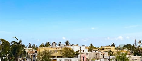 Zona residencial com vários edifícios, alguns com telhados planos e outros inclinados. Palmeiras e vegetação visíveis.