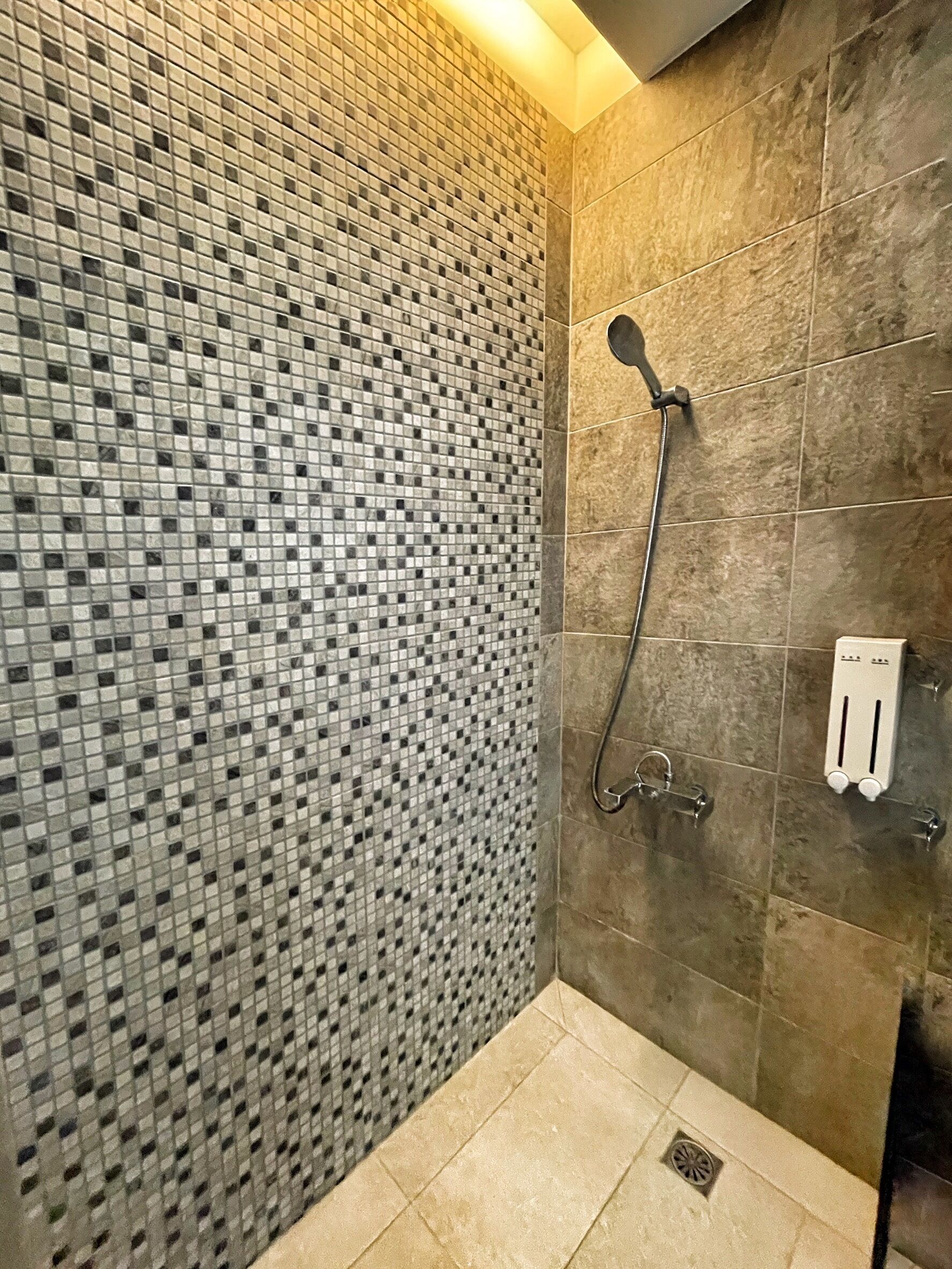 Casa de banho com azulejos em mosaico, zona de duche e porta-toalhas.