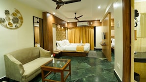 Quarto de hotel com sofá, mesa de vidro, cama com cortinas, ventilador de teto e ar condicionado.