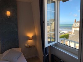 Quarto com uma grande janela com vista para a costa, uma luminária de cabeceira e uma pequena mesa de apoio.