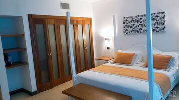 Quarto de hotel com cama, mesa de cabeceira, guarda-roupa e estante.