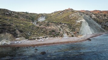 Uma praia com cadeiras de banho brancas e guarda-sóis, terreno rochoso e vista clara do mar.