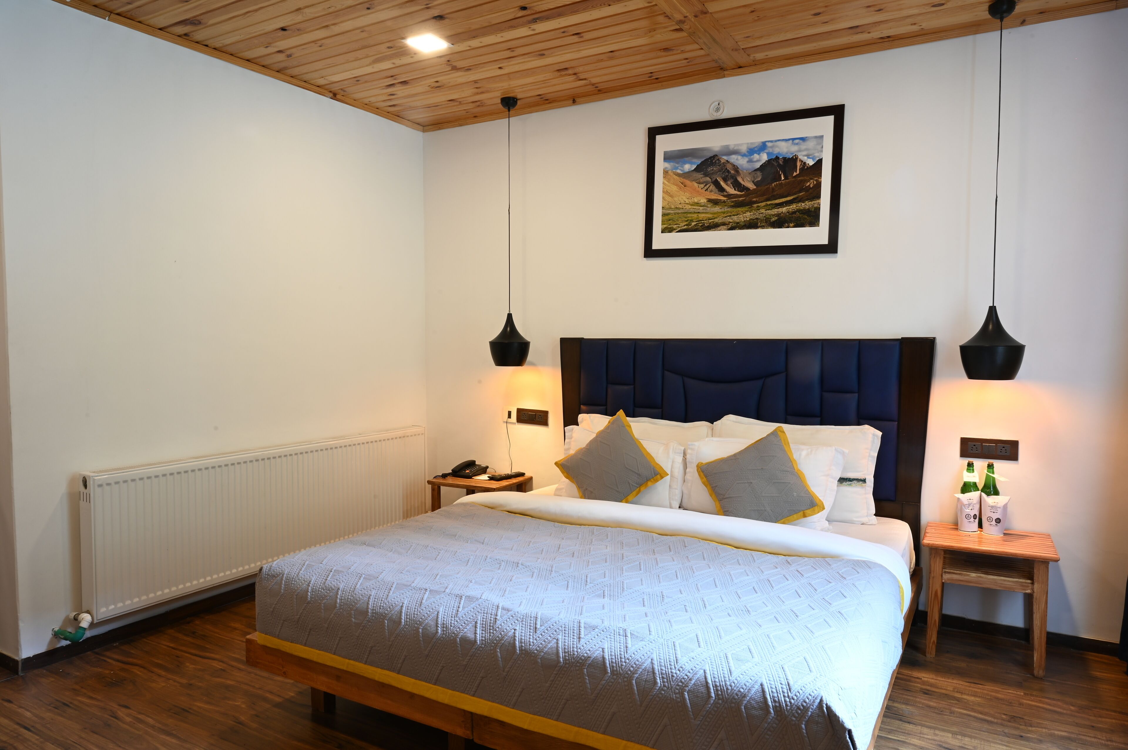 Uma cama bem arrumada com cabeceira azul, duas luminárias de apoio e um quadro na parede.