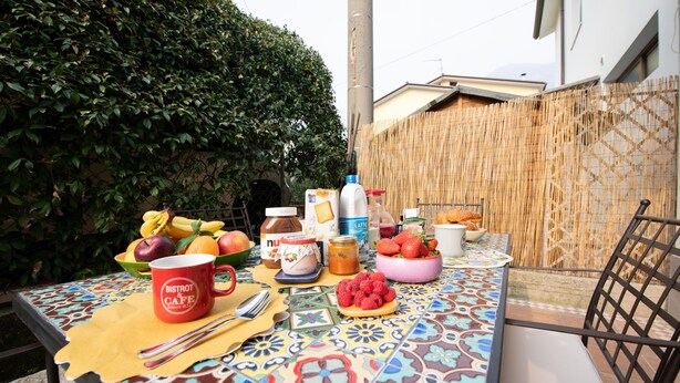 Uma mesa com toalha de mesa estampada em mosaico, diversos tipos de comida e uma caneca vermelha com a inscrição 'BISTROT CAFE'.