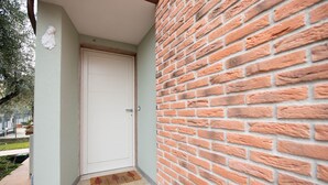 Uma porta com tapete e um pequeno degrau, além de um muro de tijolos.