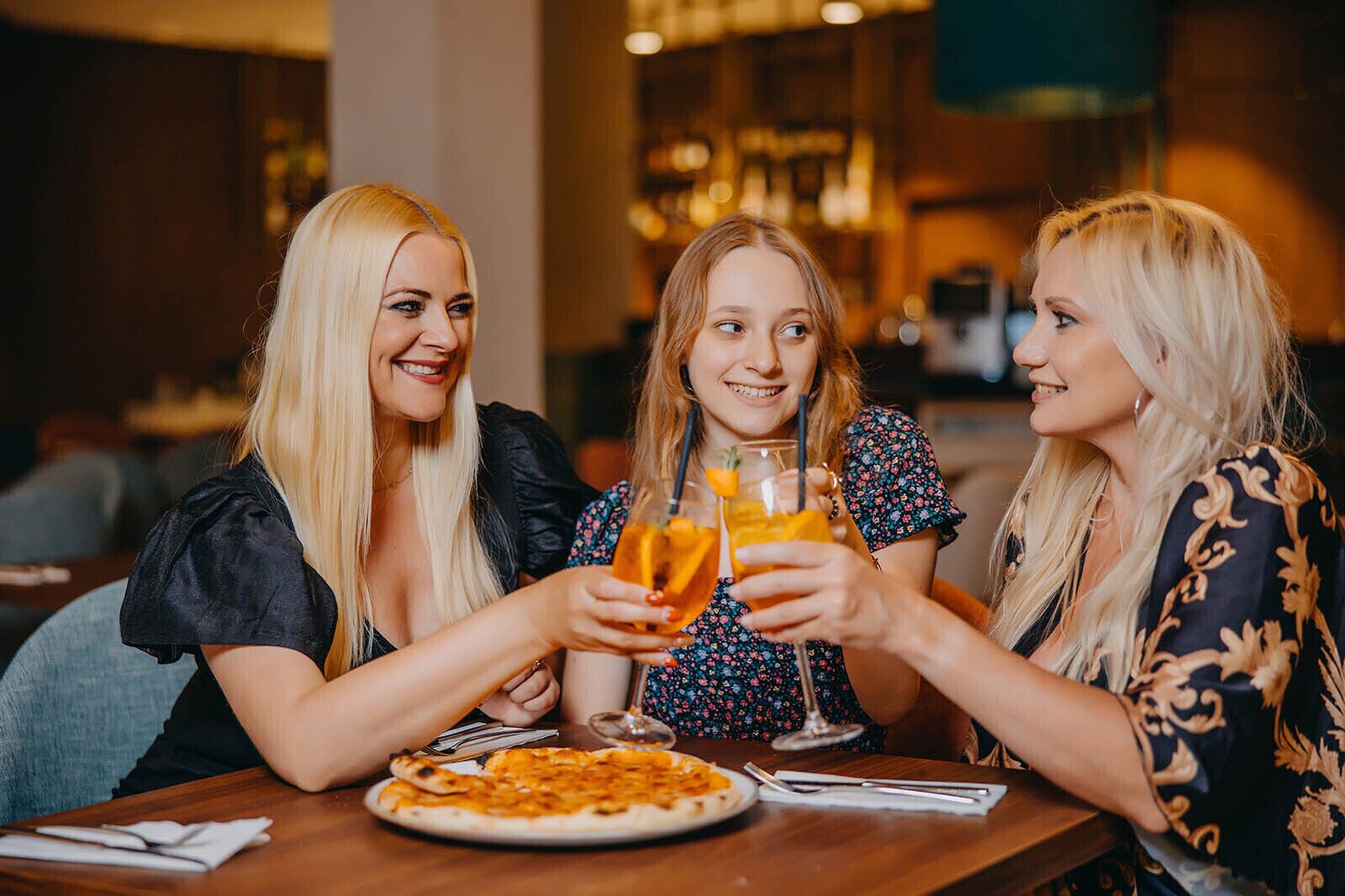 Três pessoas brindando com bebidas em uma mesa com pizza.