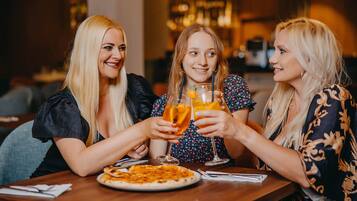 Três pessoas brindando com bebidas em uma mesa com pizza.