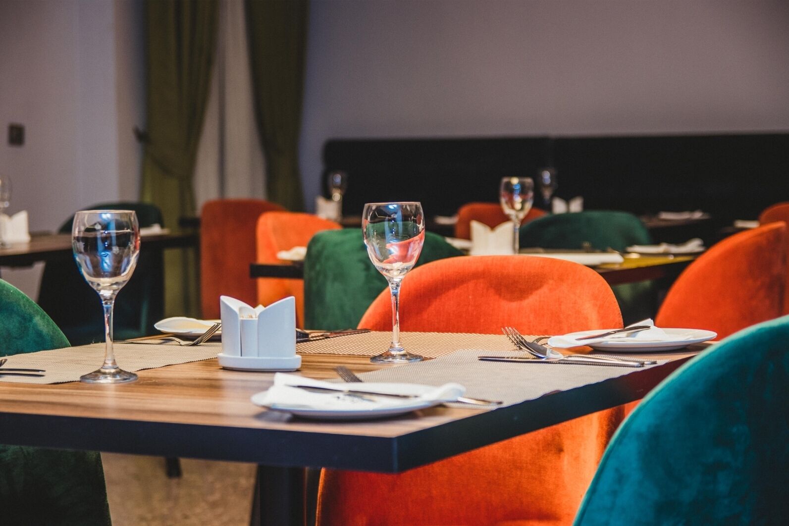 Uma área de refeições com mesas preparadas para dois, cada uma com uma taça de vinho, talheres e um menu.