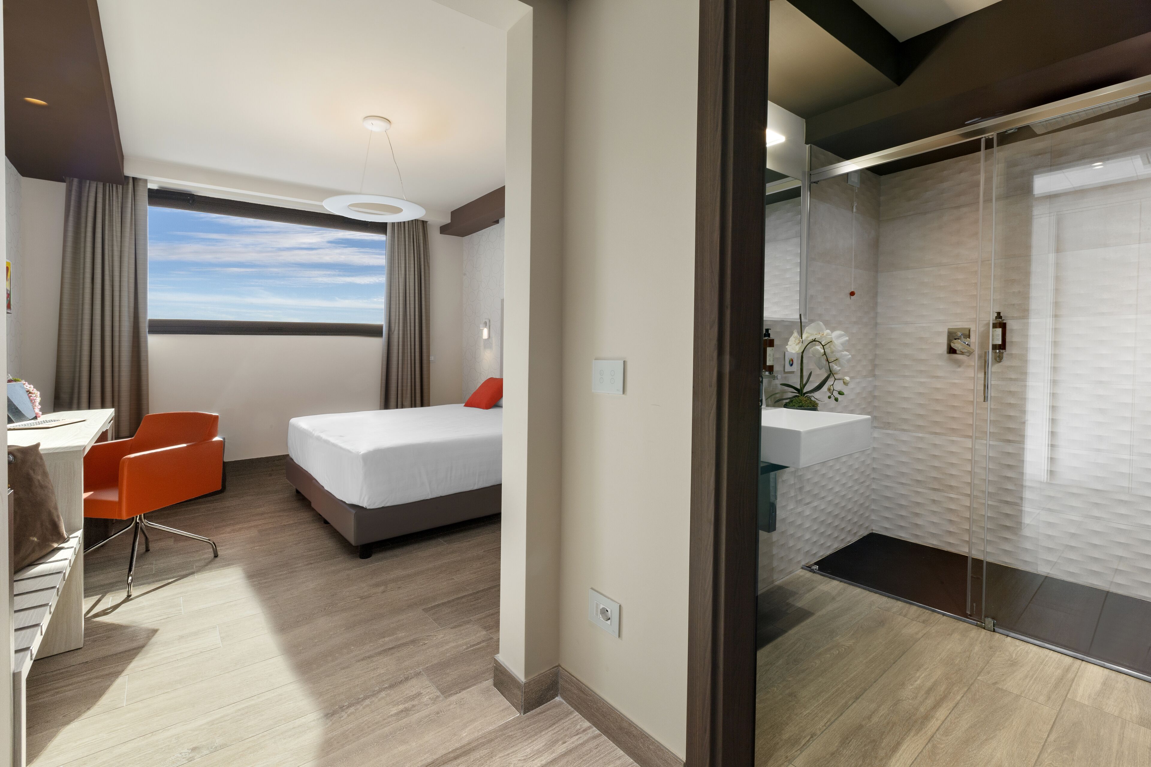 Quarto de hotel moderno com cama, escrivaninha e área de chuveiro.