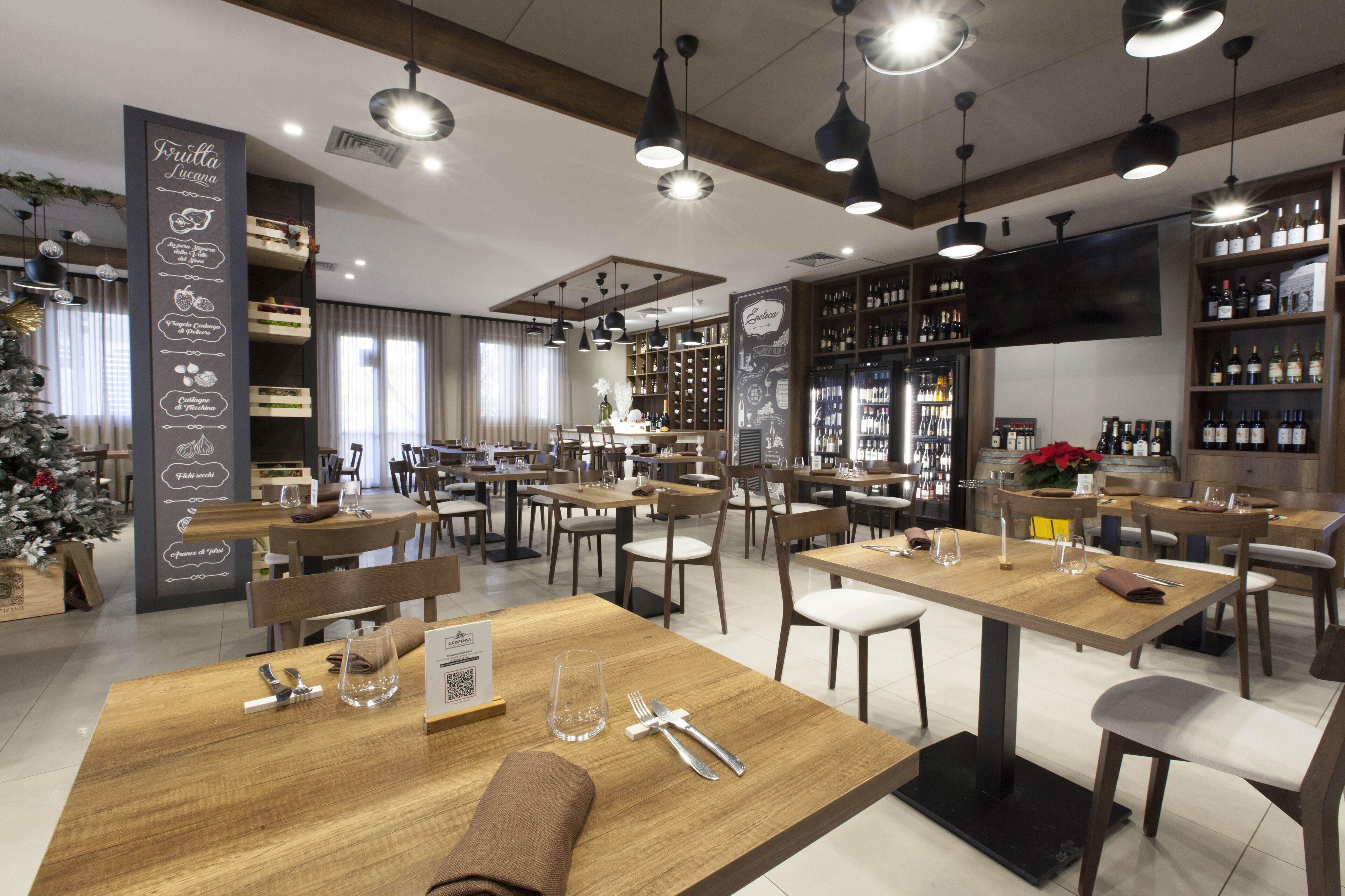 Um restaurante com mesas e cadeiras de madeira, um pinheiro de Natal e uma estante para vinhos.