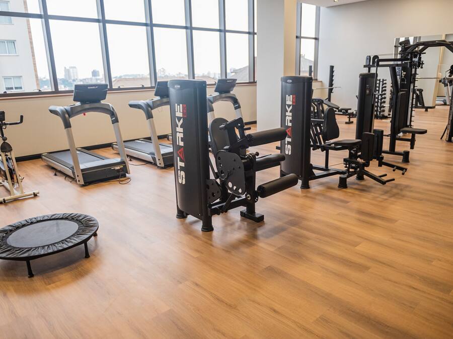 Uma academia com esteiras, máquinas de musculação e um trampolim.