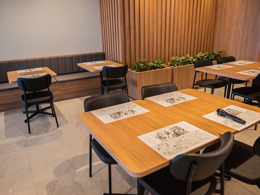 Sala de conferência com mesas de madeira e cadeiras pretas, equipada com cartões de identificação e uma tela de projeção.