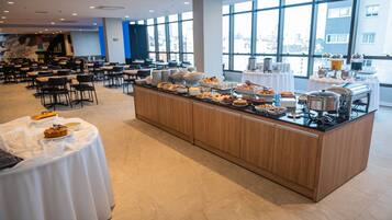 Buffet com diversos alimentos e vista para a cidade através de grandes janelas.