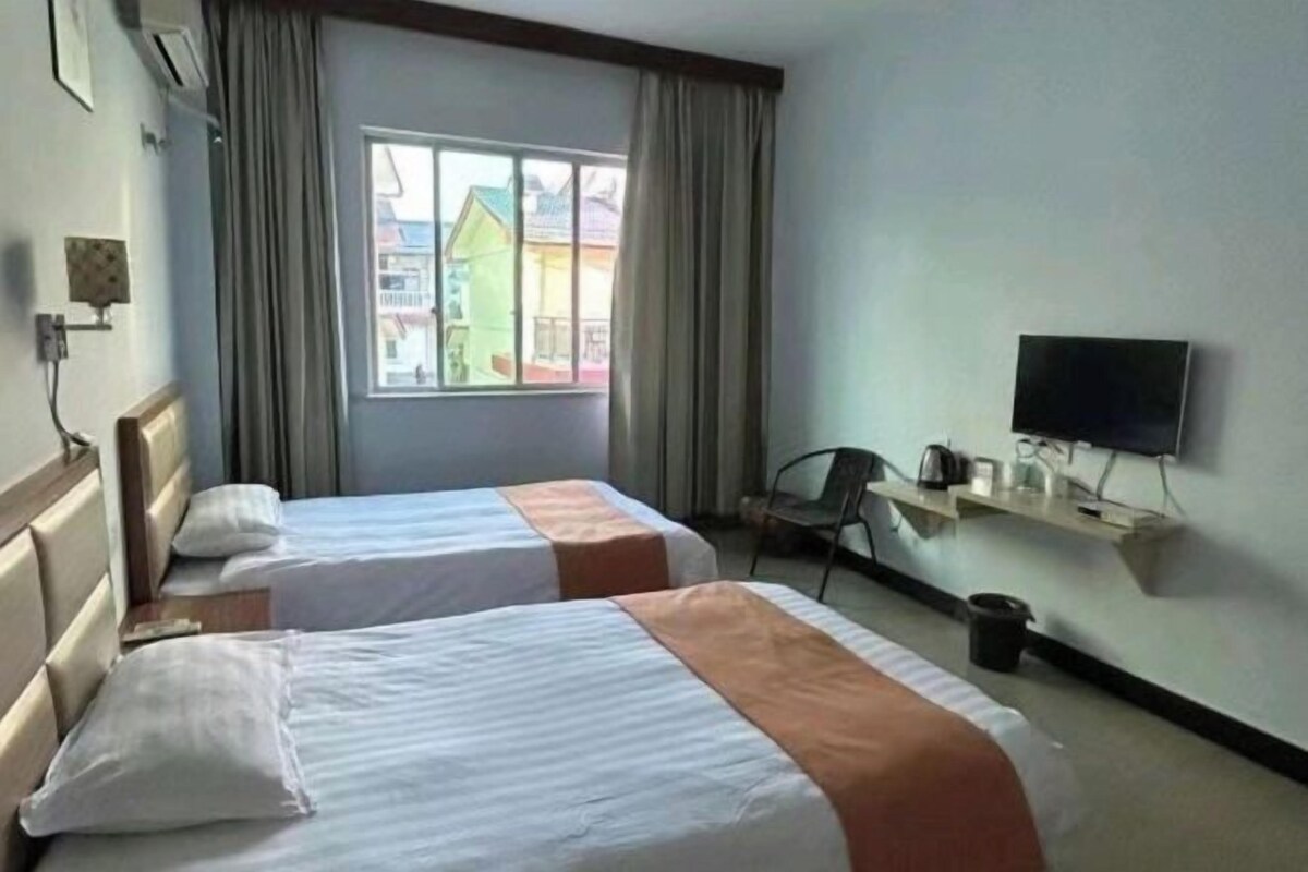 Quarto de hotel com duas camas, televisão, secretária e janela com cortinas.