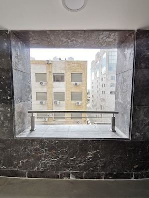 Visão pela janela com moldura de metal, mostrando um edifício com vários aparelhos de ar condicionado e guarda-corpo de varanda.