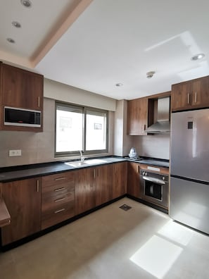 Cozinha moderna com armários de madeira, eletrodomésticos de aço inoxidável e uma janela que traz luz natural.