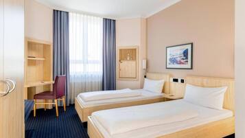 Quarto de hotel com duas camas, uma escrivaninha, uma cadeira e uma janela com cortinas.