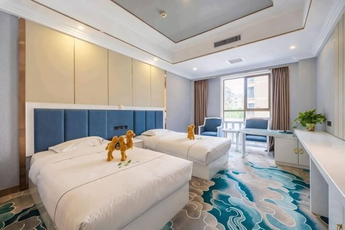 Quarto de hotel com duas camas, uma escrivaninha, uma cadeira e vista para o exterior.