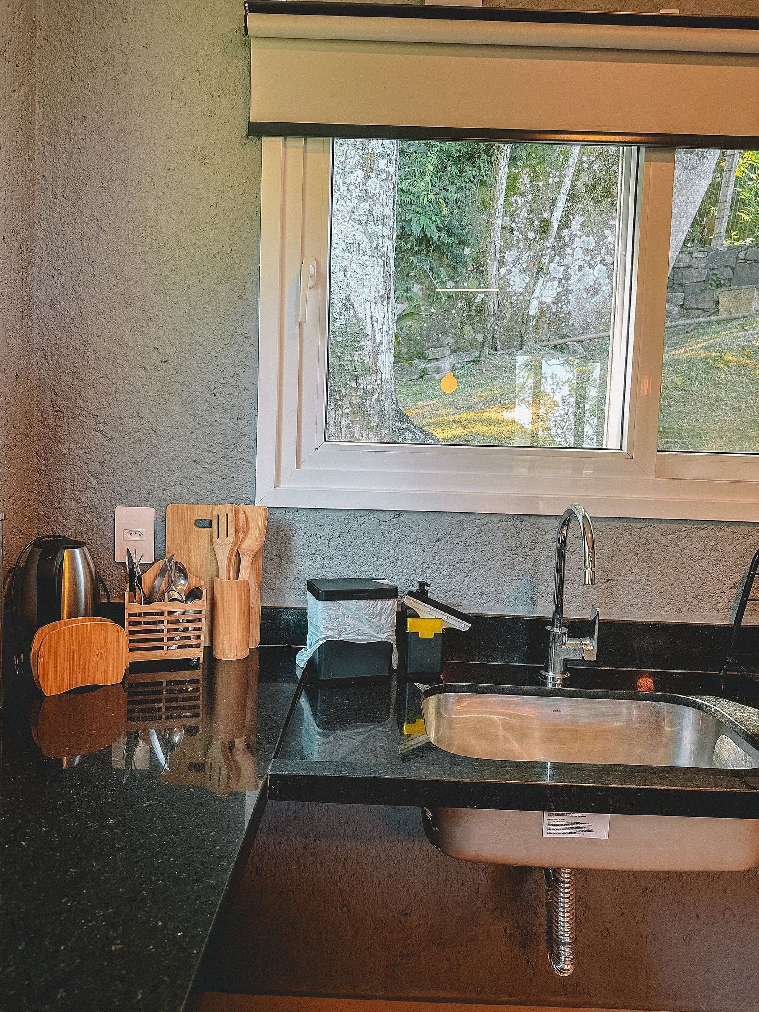 Cozinha com pia, janela e vista para árvores lá fora.