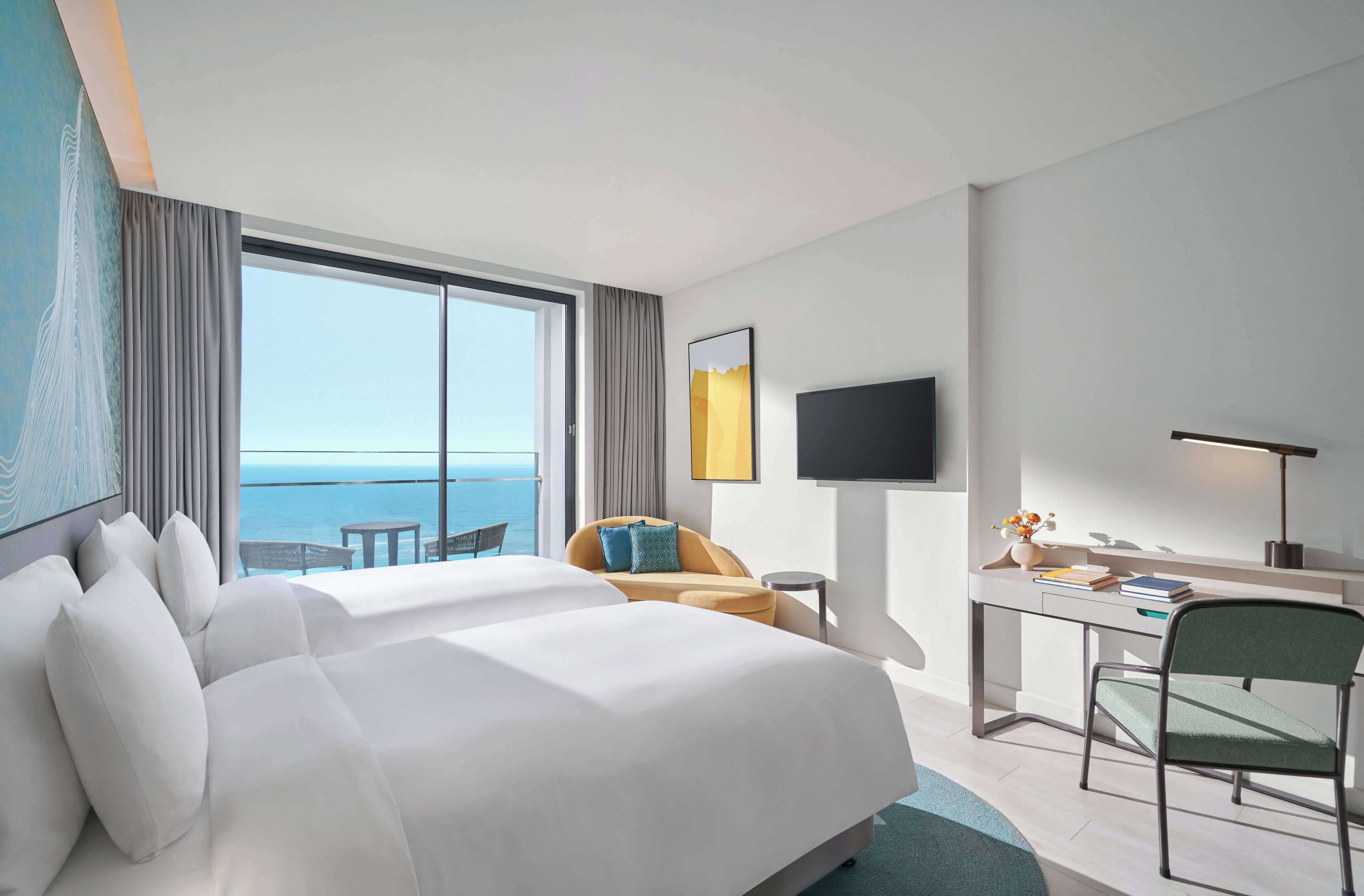 Quarto de hotel com uma cama grande, uma escrivaninha com cadeira, uma televisão e vista para o oceano.