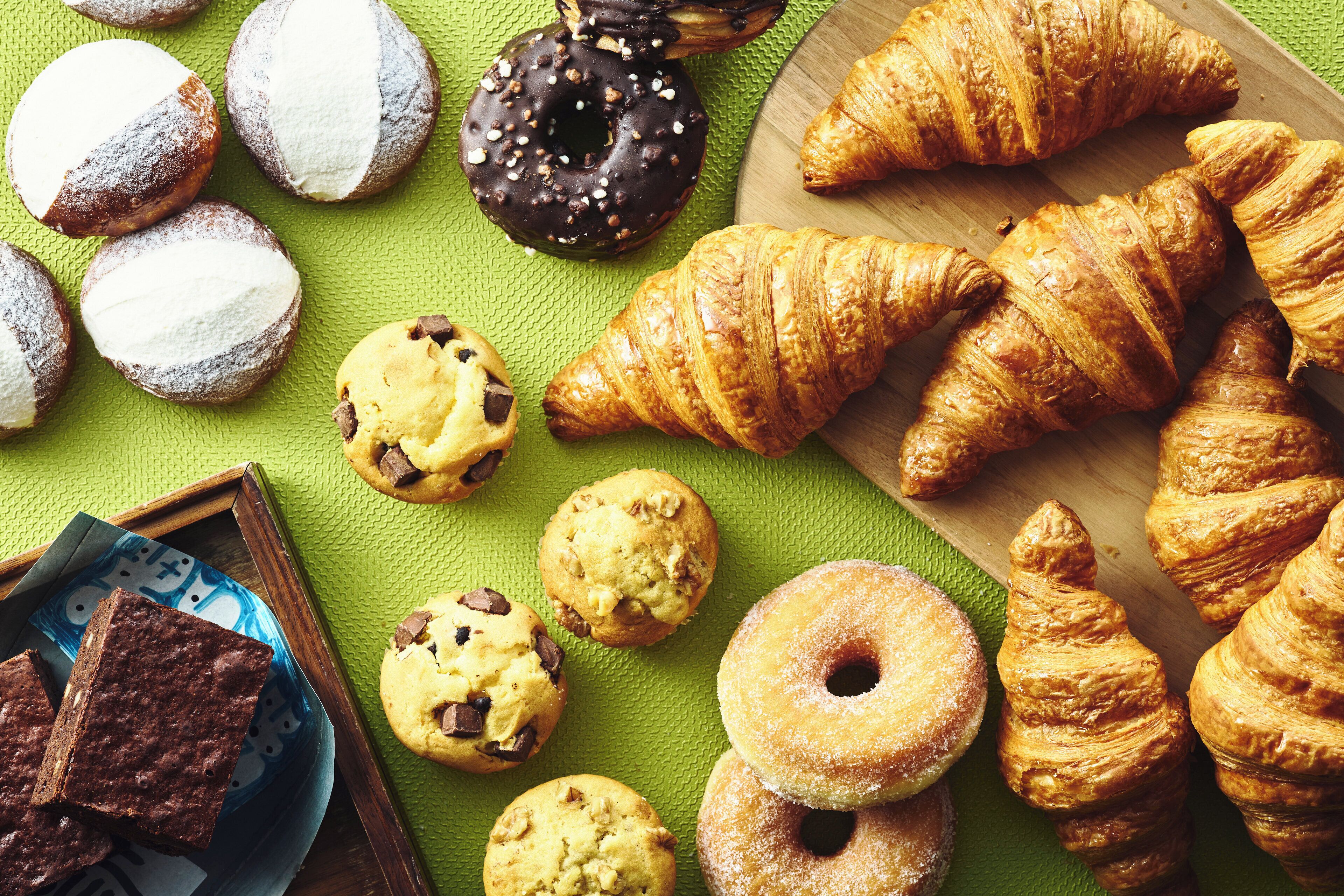 Diversos produtos de panificação, incluindo bolachas, sonhos cobertos de chocolate e croissants.