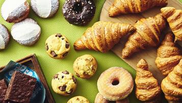 Diversos produtos de panificação, incluindo bolachas, sonhos cobertos de chocolate e croissants.