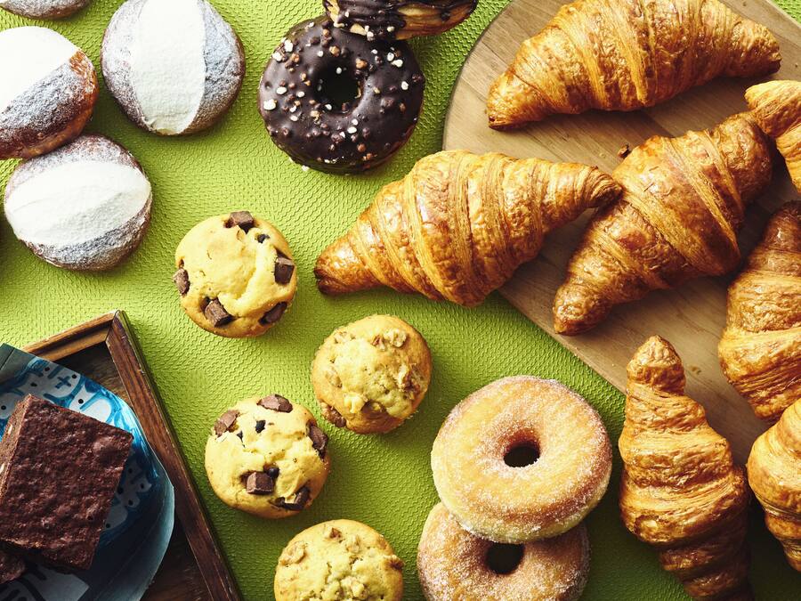 Diversos produtos de panificação, incluindo bolachas, sonhos cobertos de chocolate e croissants.