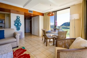 Ampla sala de estar com mesa de jantar posta para quatro pessoas, sofá e vista para o exterior.